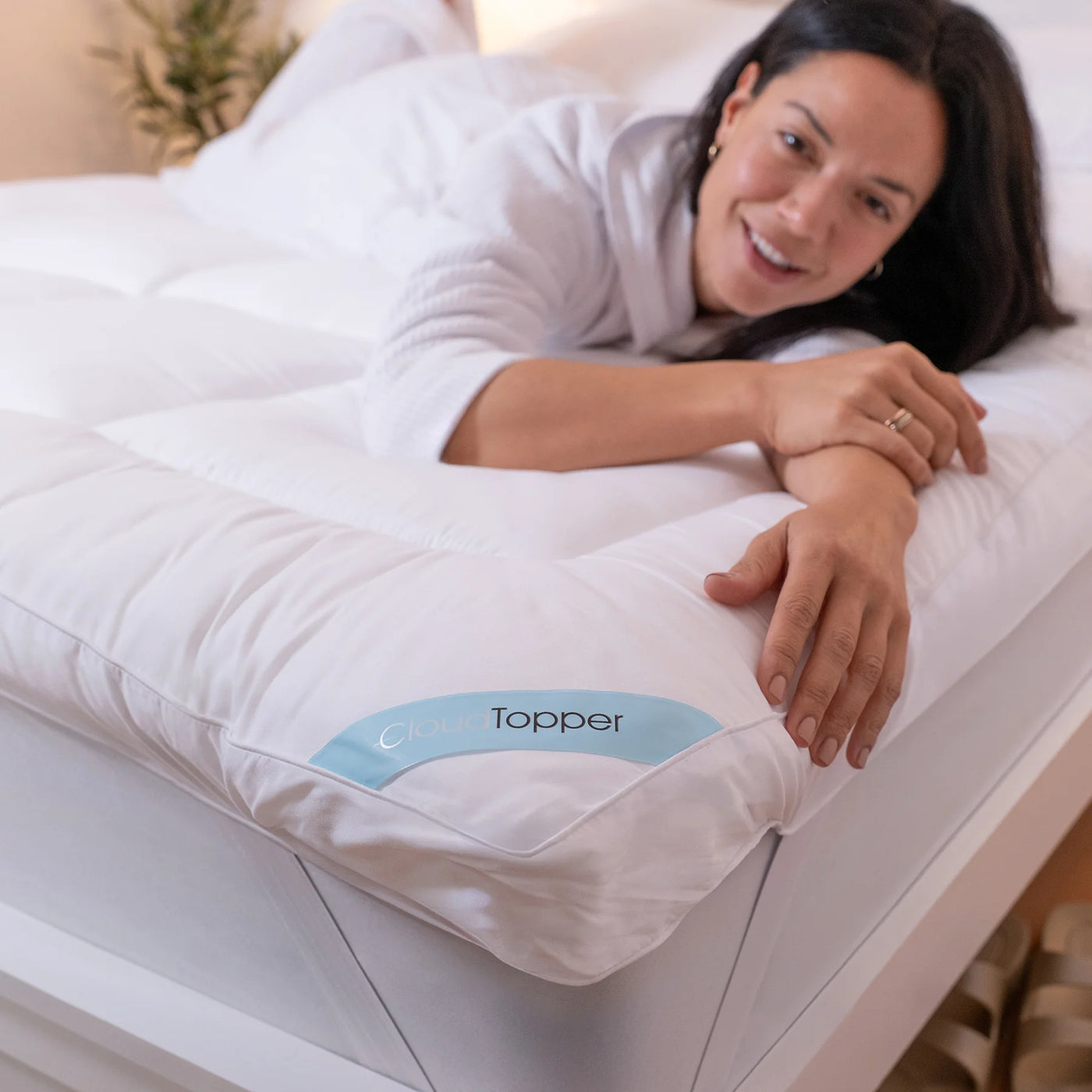 Woman lying on a bed with a white mattress topper labeled 'Topper'.